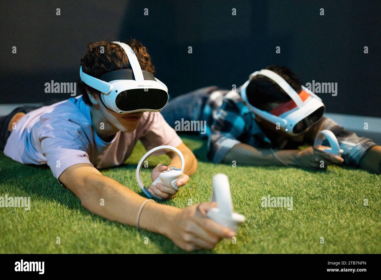 A young man lies prone on artificial grass, engaged in virtual reality ...