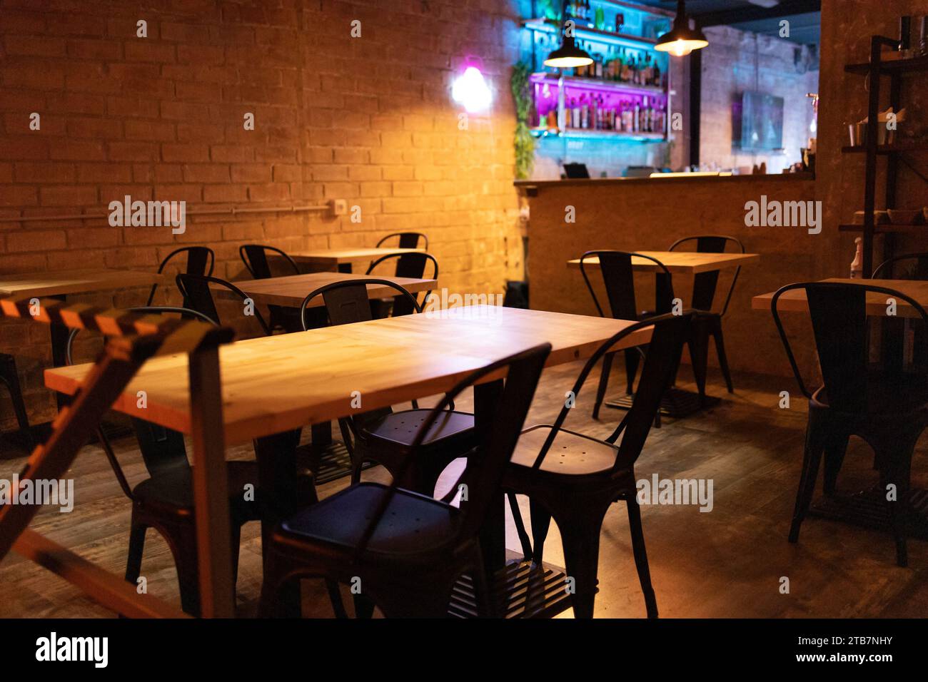 An empty cozy bar interior with wooden tables, metal chairs, and a warm ...