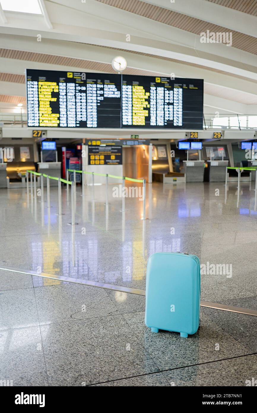 Blue trolley bag on tiled floor with arrival departure board in ...