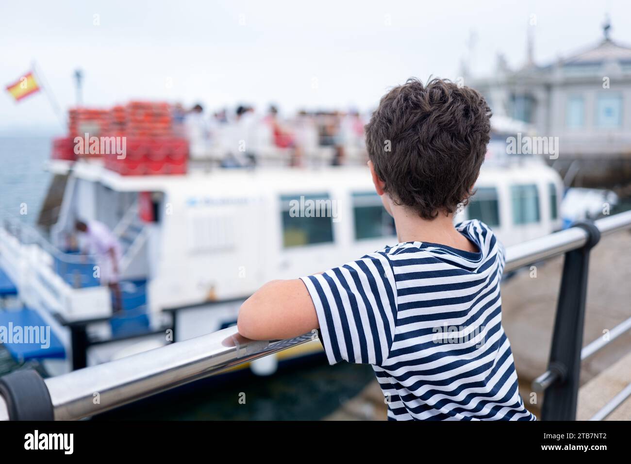 Back view of unrecognizable boy in shirt watching a ferry from the port ...