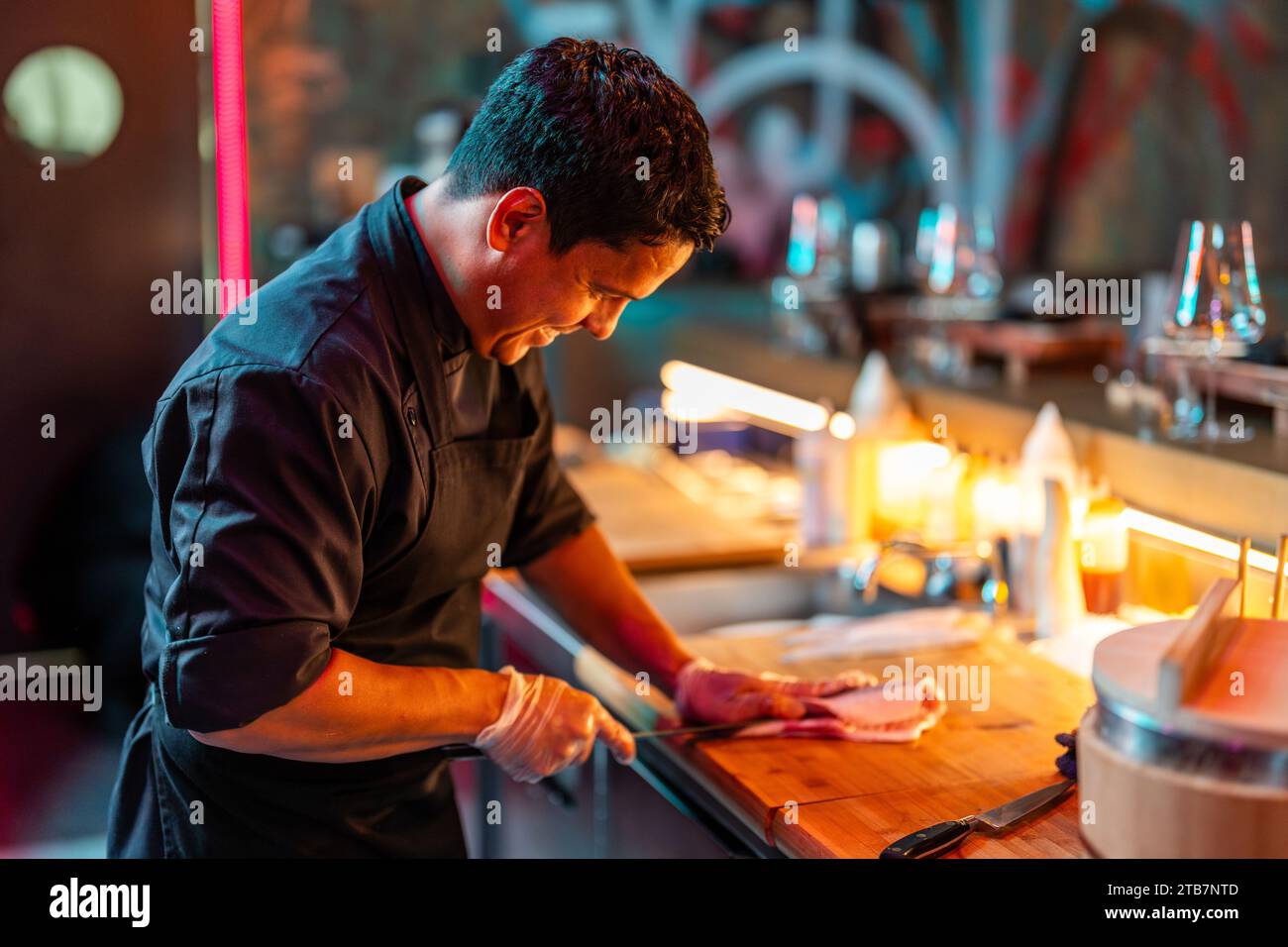 Side view of smiling male chef wearing gloves and black uniform slicing ...