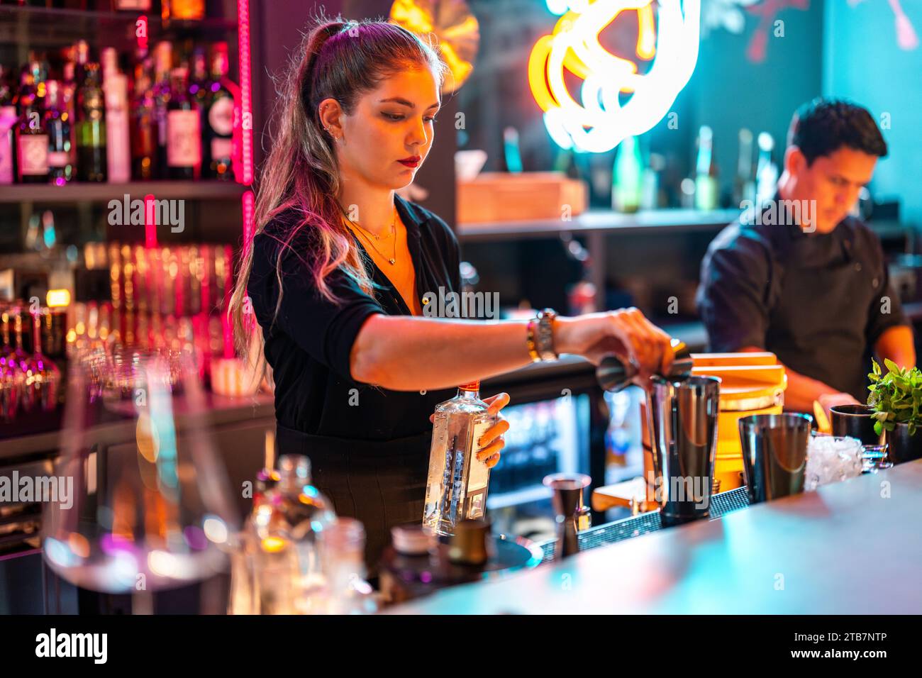 Young beautiful Caucasian barmaid in black uniform pouring liquor from ...