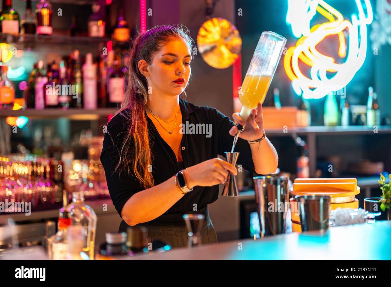 Confident beautiful young barkeeper pouring alcohol in jigger from ...