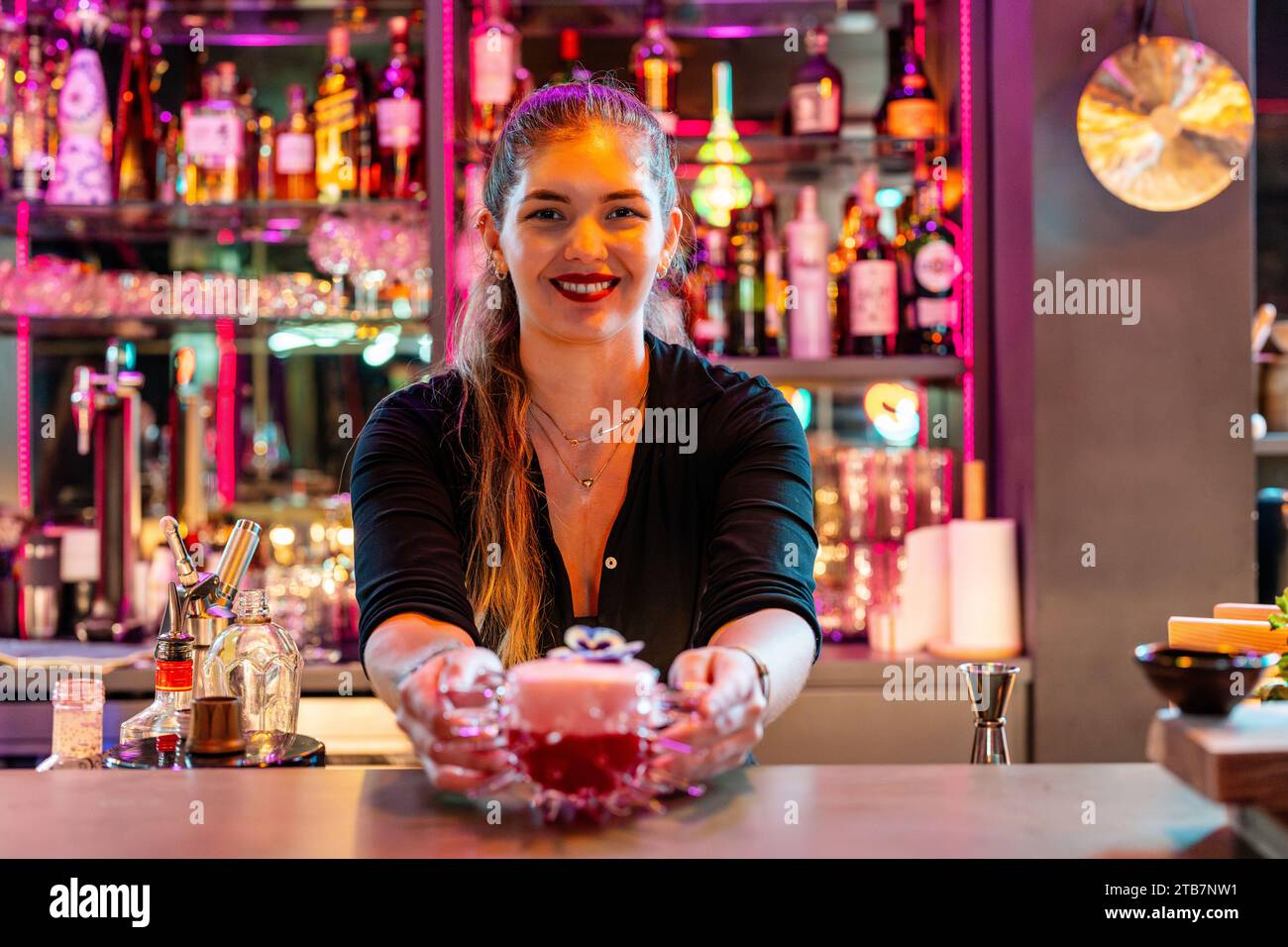 Happy beautiful young barmaid in black uniform smiling at camera while ...