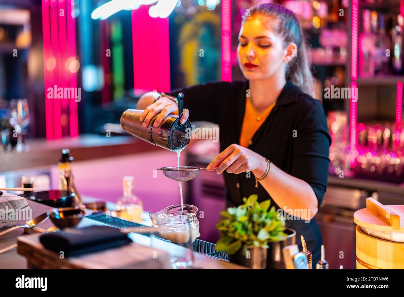Beautiful confident young female barkeeper standing while straining ...