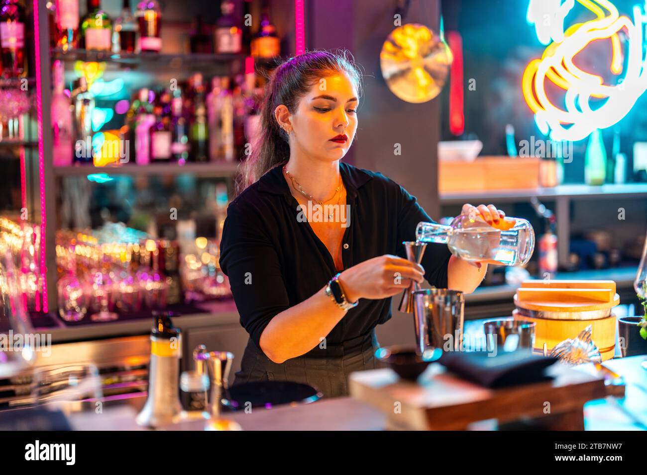 Confident beautiful young barkeeper pouring alcohol in jigger from ...