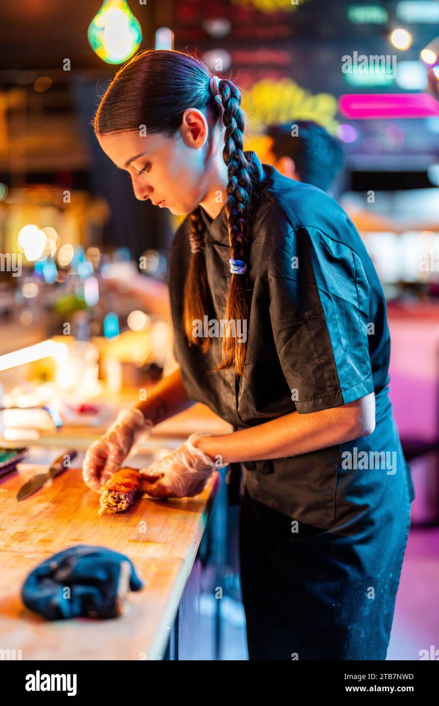 Side view of young female cook dressed in black uniform and gloves with ...