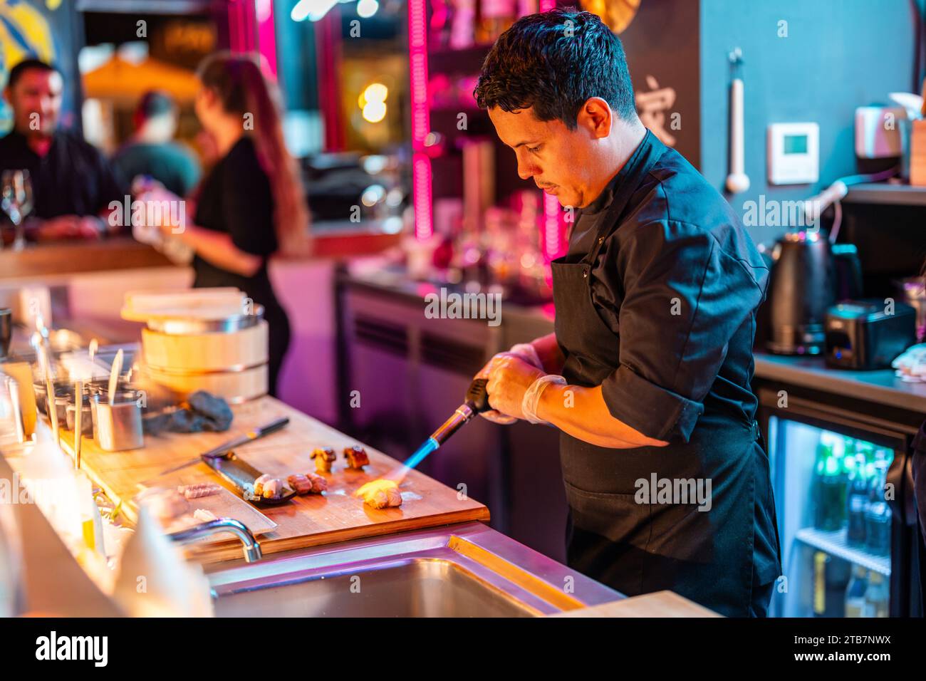 Side view of confident focused male cook in black uniform using blow ...