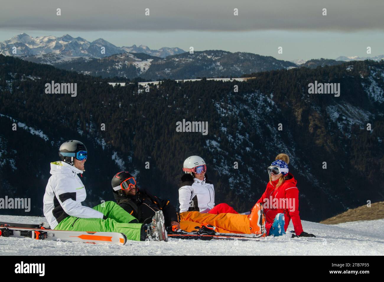 A cheerful group of skiers in colorful outfits takes a break on the ...