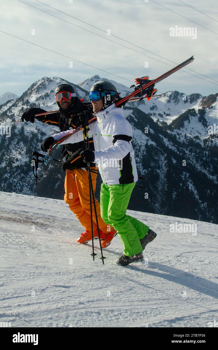 A pair of skiers carrying their equipment traverse a snowy slope with ...