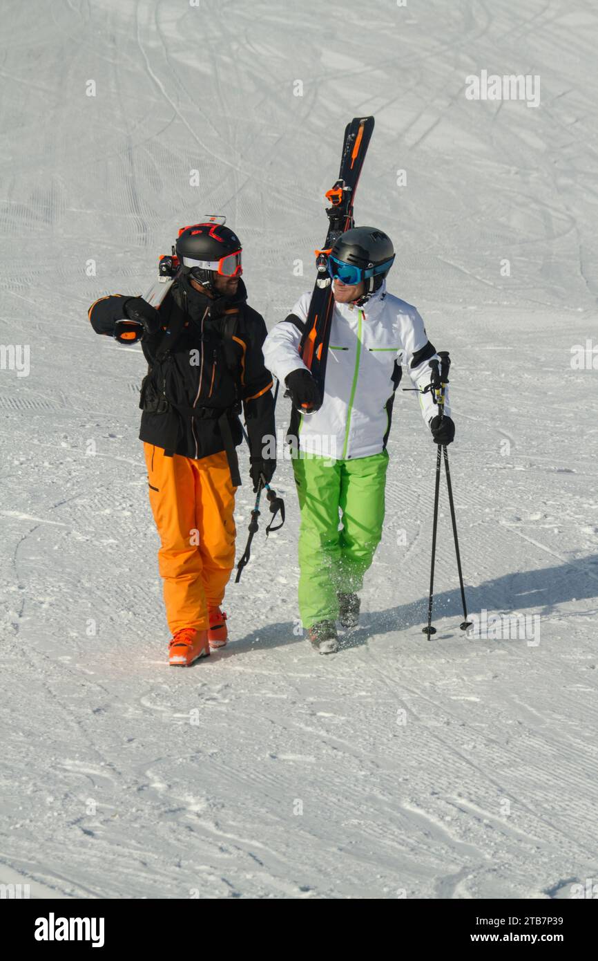 Two skiers clad in colorful gear walk through freshly groomed snow in ...