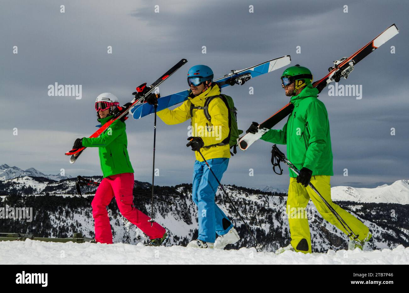Three friends, clad in colorful ski gear, carrying their skis, joyfully ...