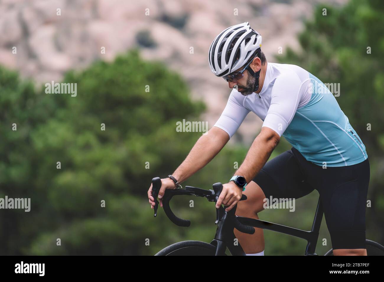 Side view of cyclist in a white and blue jersey riding a road bike in a ...