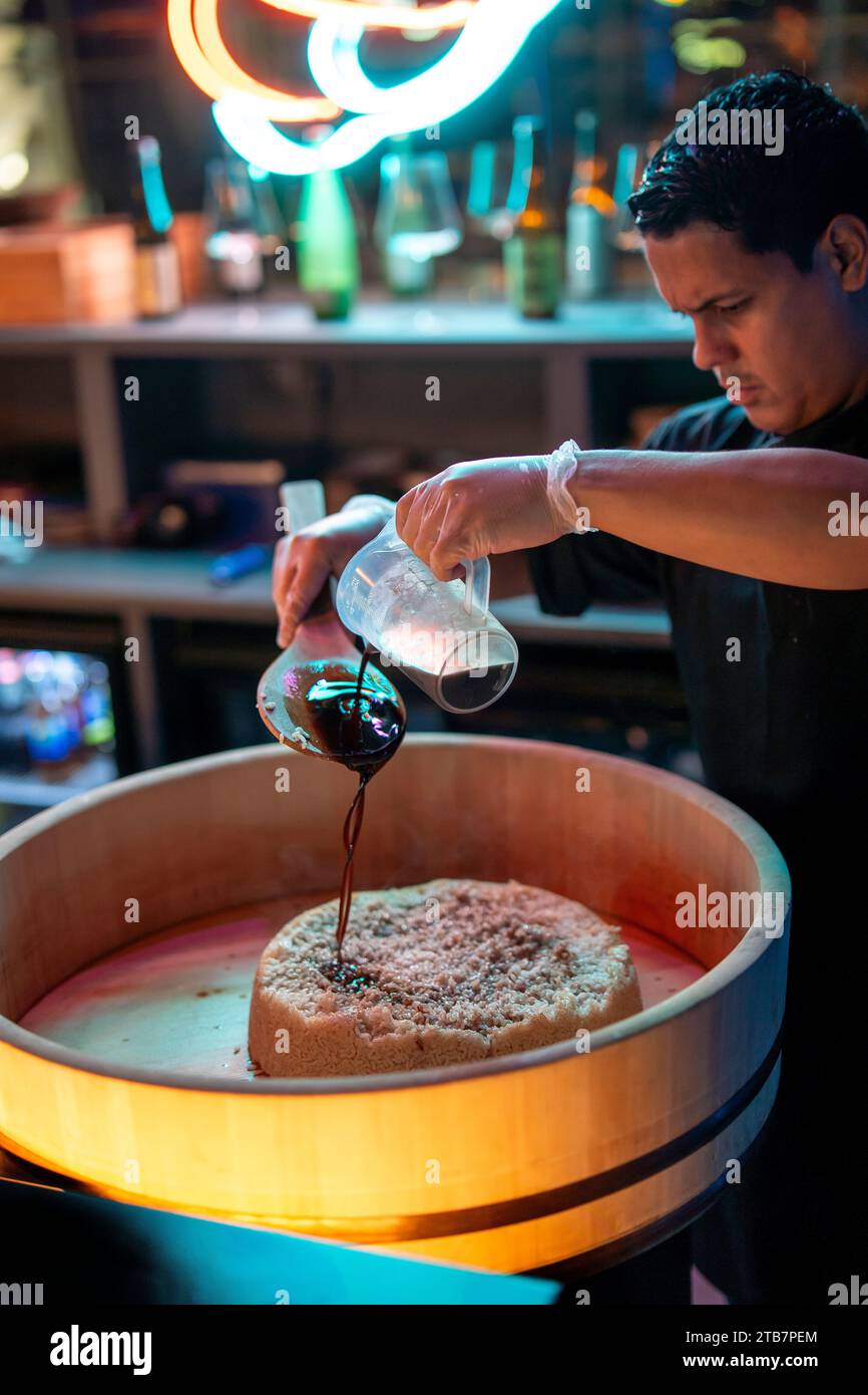 A focused chef is seen mixing sushi rice in a wooden tub called hangiri ...
