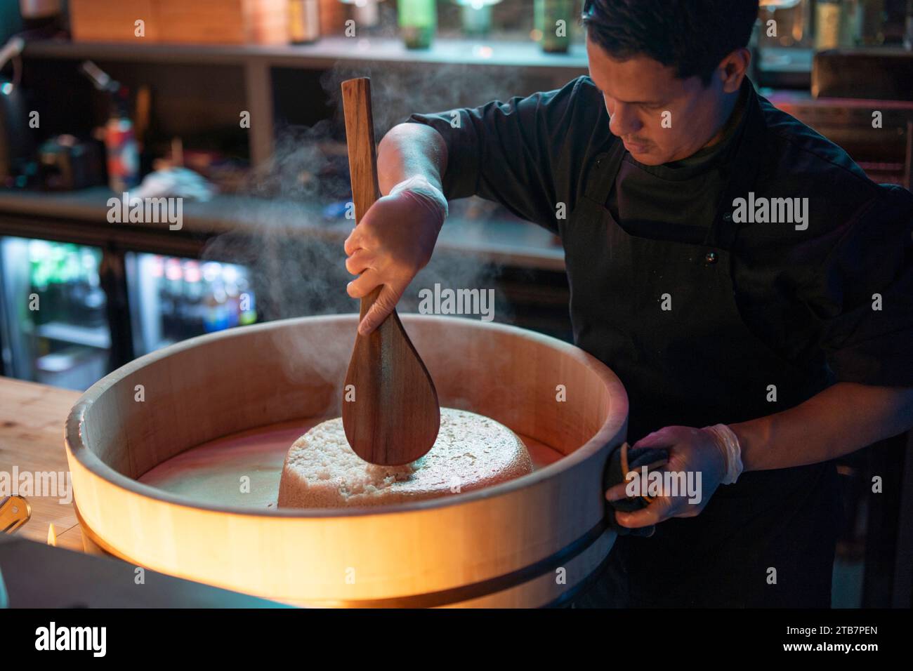 An expert sushi chef carefully mixes sushi rice in a wooden tub known ...