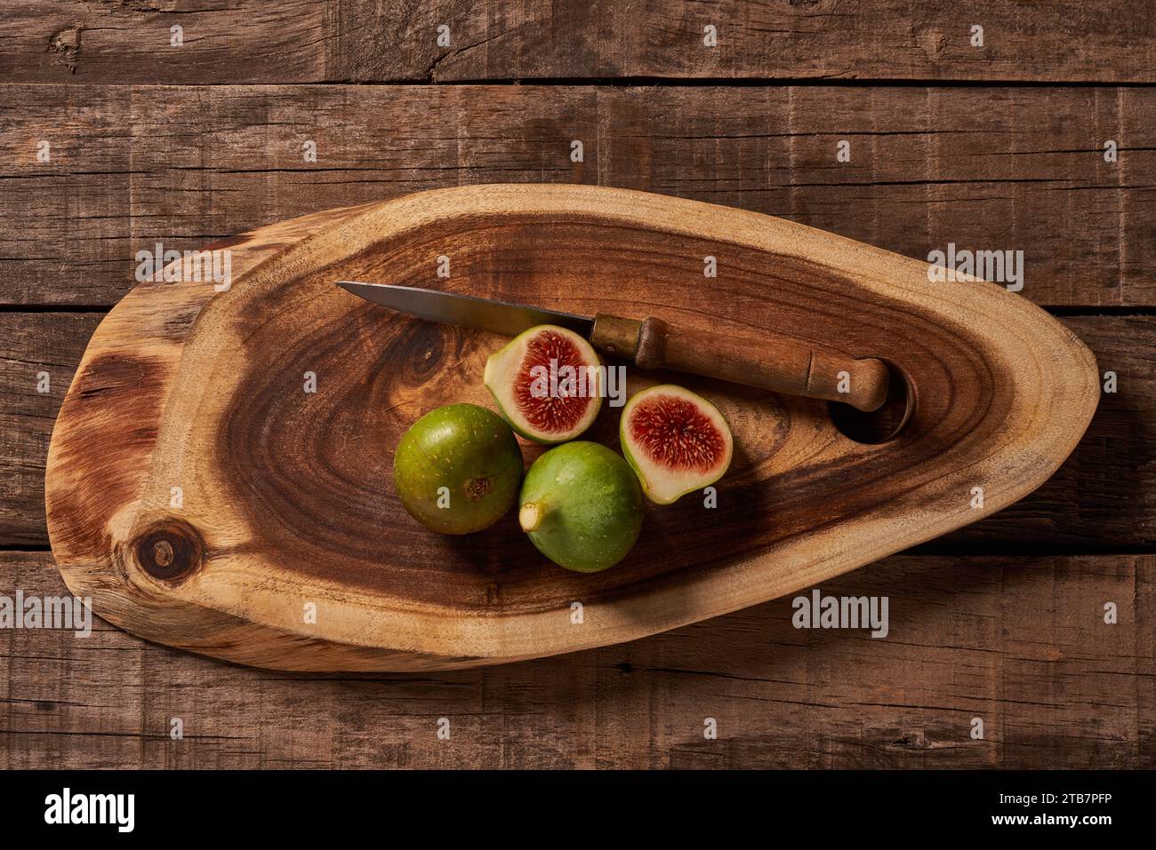 A rustic scene of fresh green figs, one sliced open, on an oval wooden ...