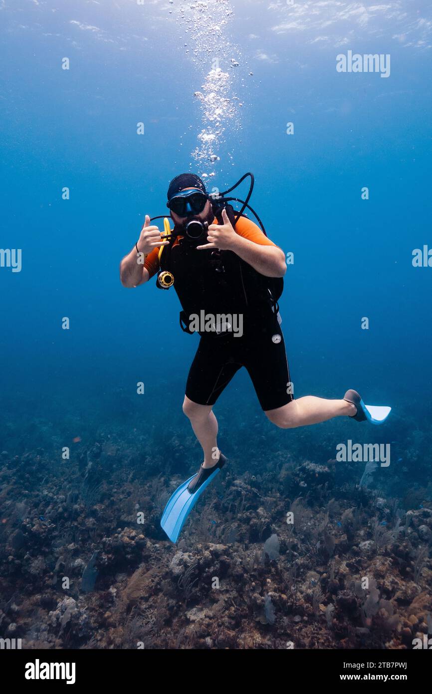 A male scuba diver hovers weightlessly above a coral reef in clear blue ...