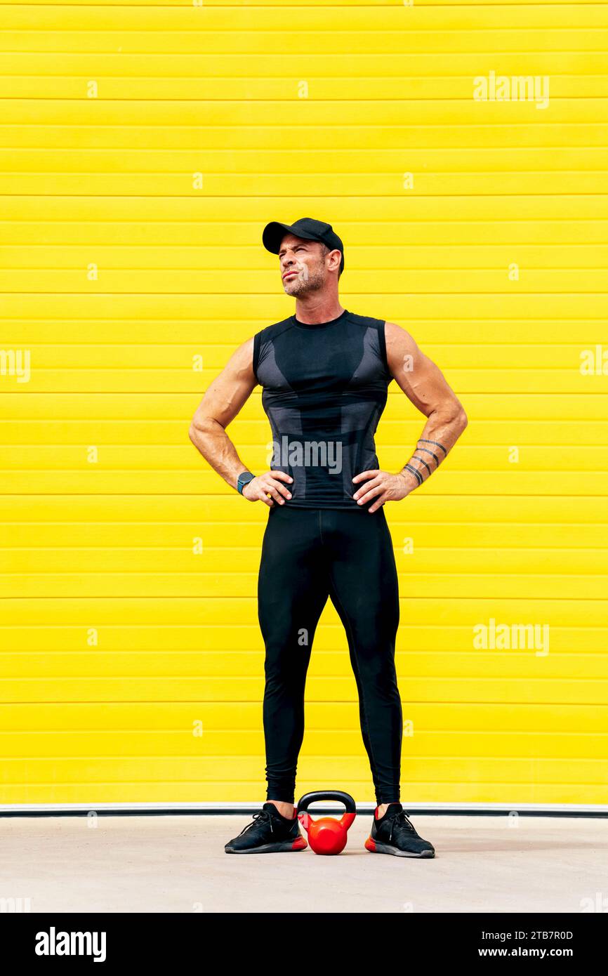 Muscular male athlete with arms akimbo standing with kettlebell on ...
