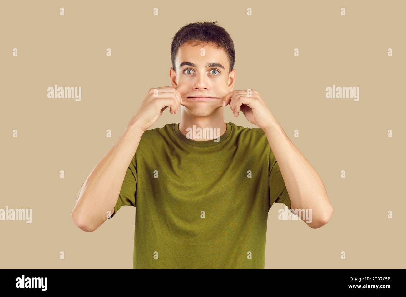 Studio portrait of young grimacing boy in green t-shirt on beige ...