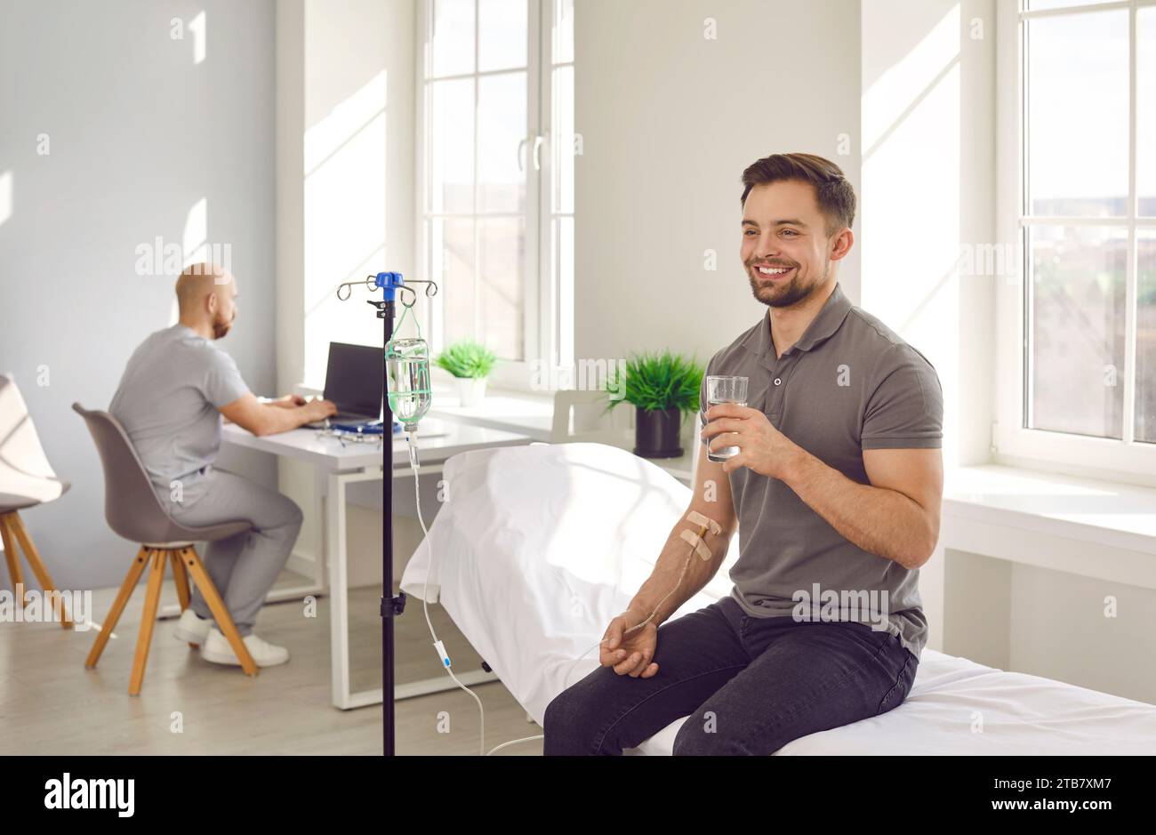 Happy man sitting at doctor's office in clinic while receiving IV drip ...