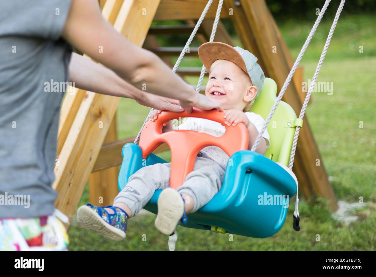 Mother pushing her infant baby boy child on a swing on playground ...