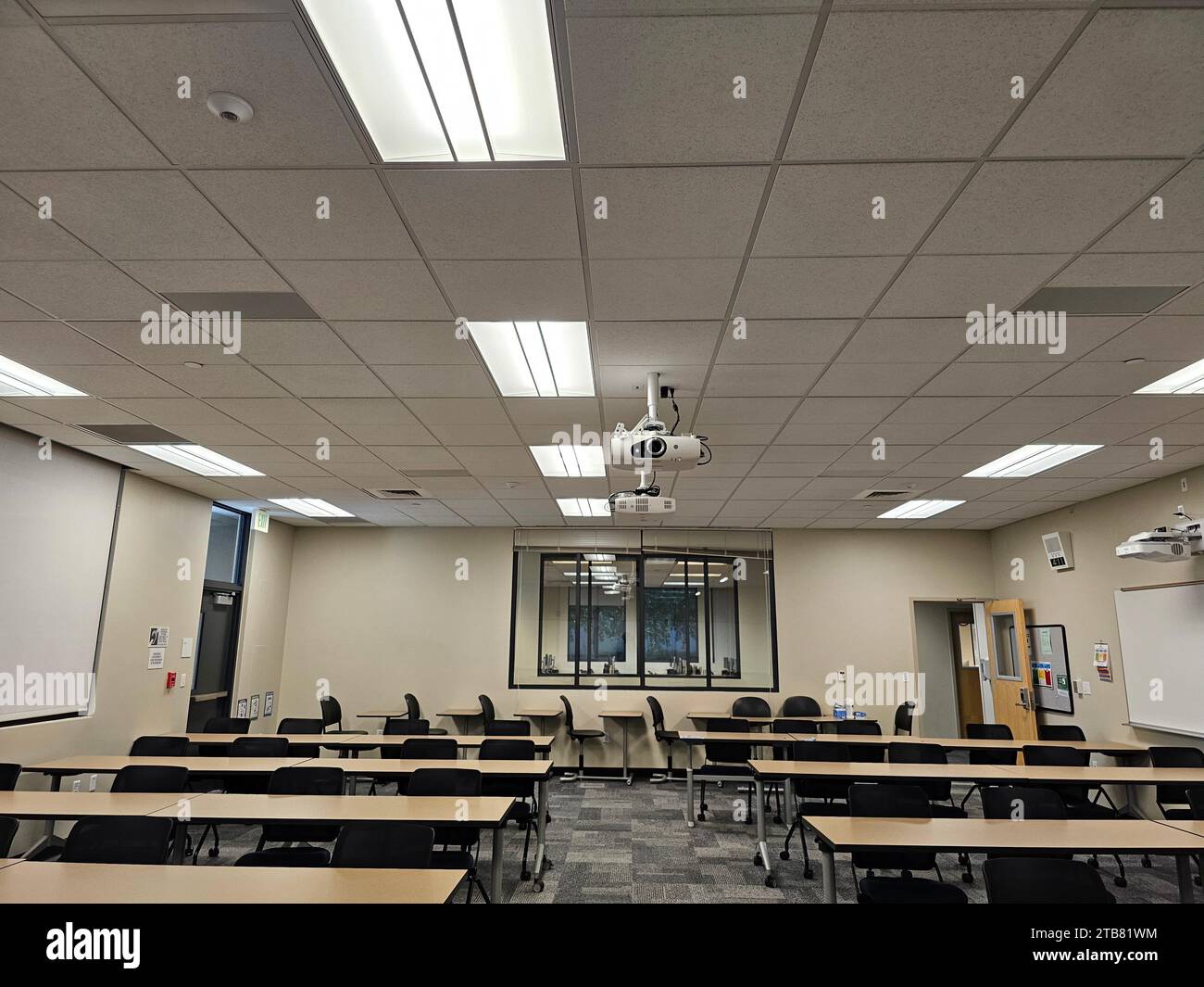 An empty classroom interior, with rows of desks and a projector suspended from the ceiling Stock ...