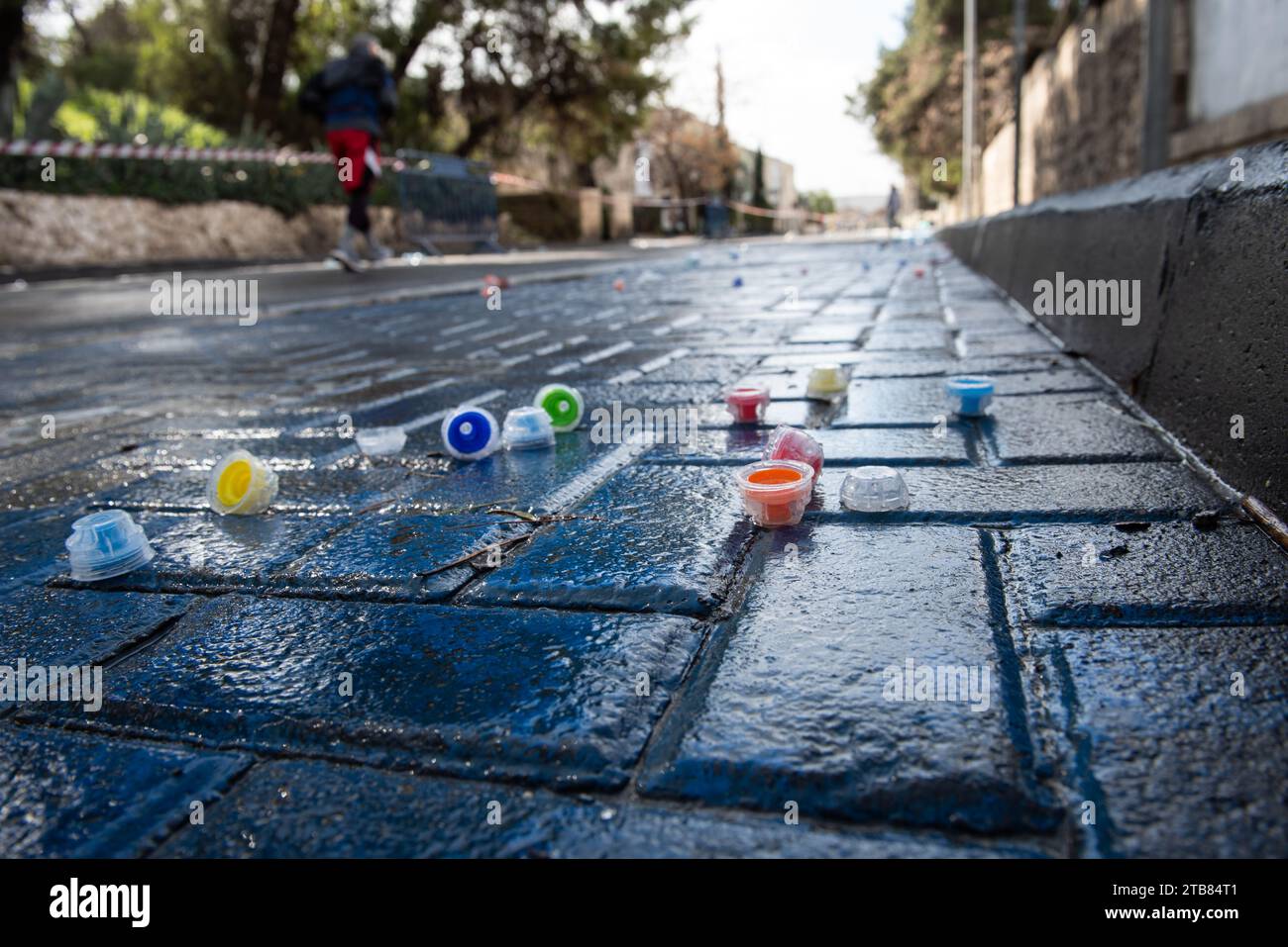 Multi-colored plastic water bottle caps lie on a wet, cobblestone ...