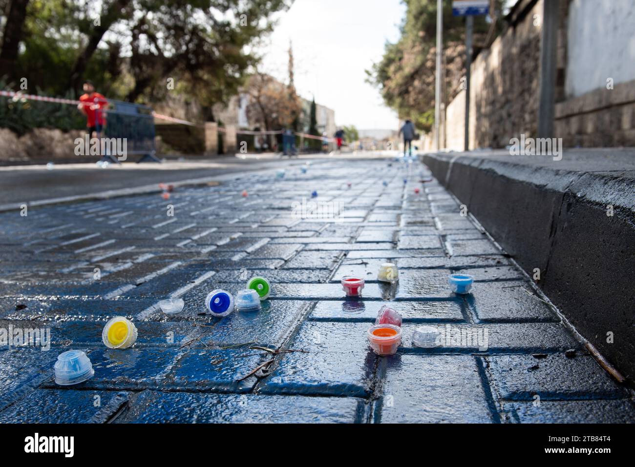 Multi-colored plastic water bottle caps lie on a wet, cobblestone ...