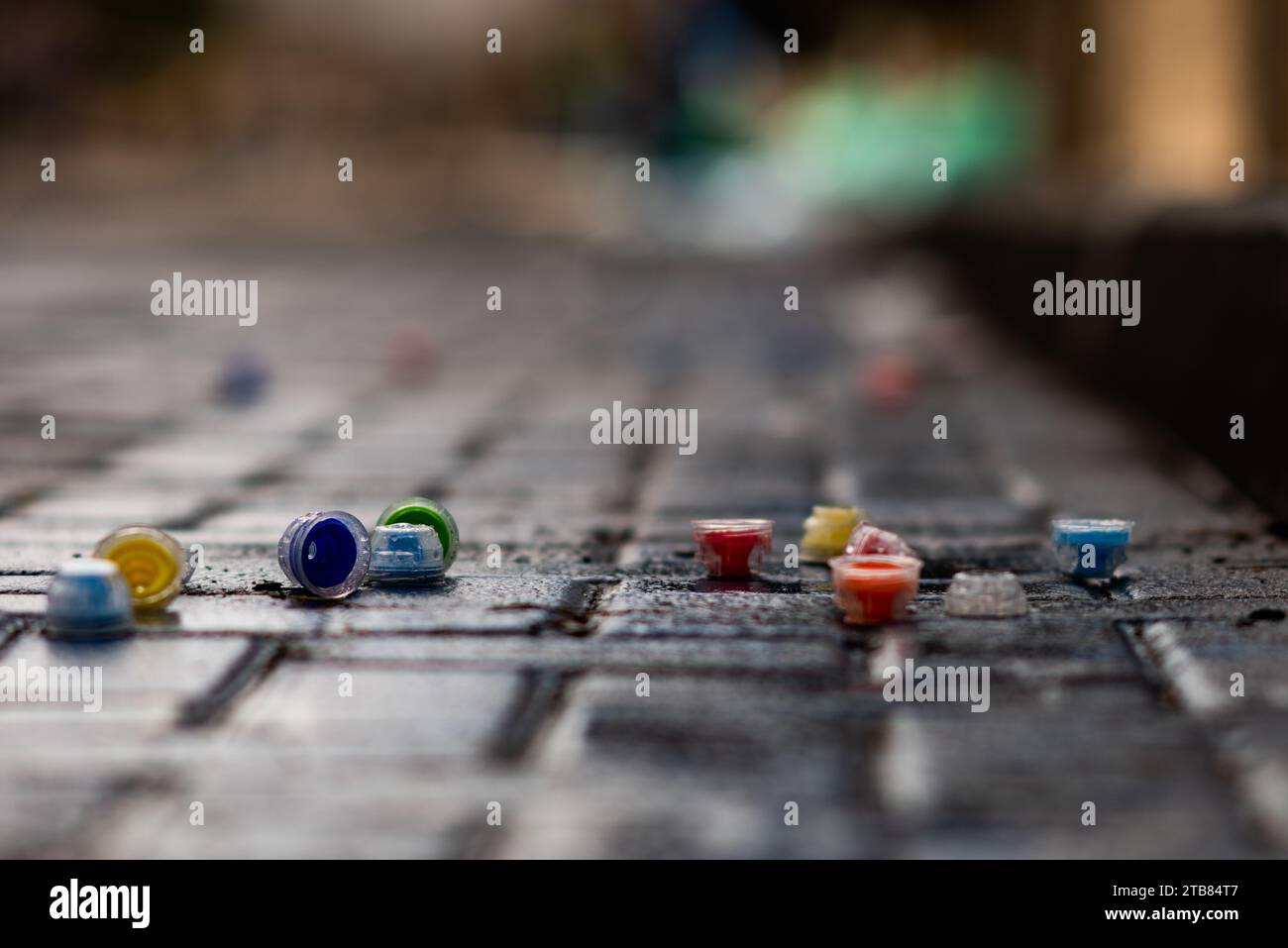 Multi-colored plastic water bottle caps lie on a wet, cobblestone ...