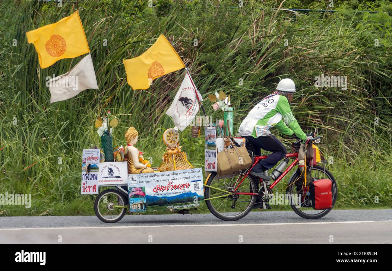 Ayutthaya, THAILAND, SEP 30 2023, A cyclist pulls a cart with a Buddha ...