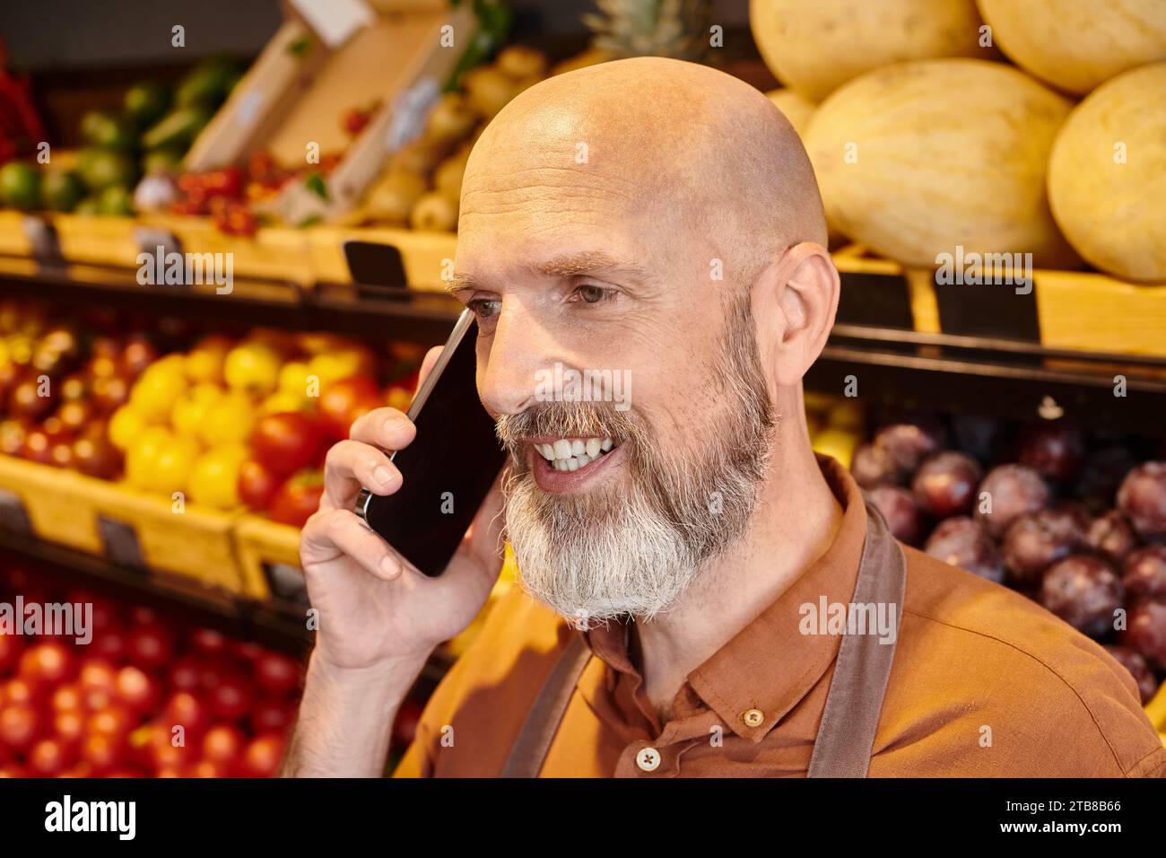 cheerful mature salesman talking actively by phone with blurred grocery ...