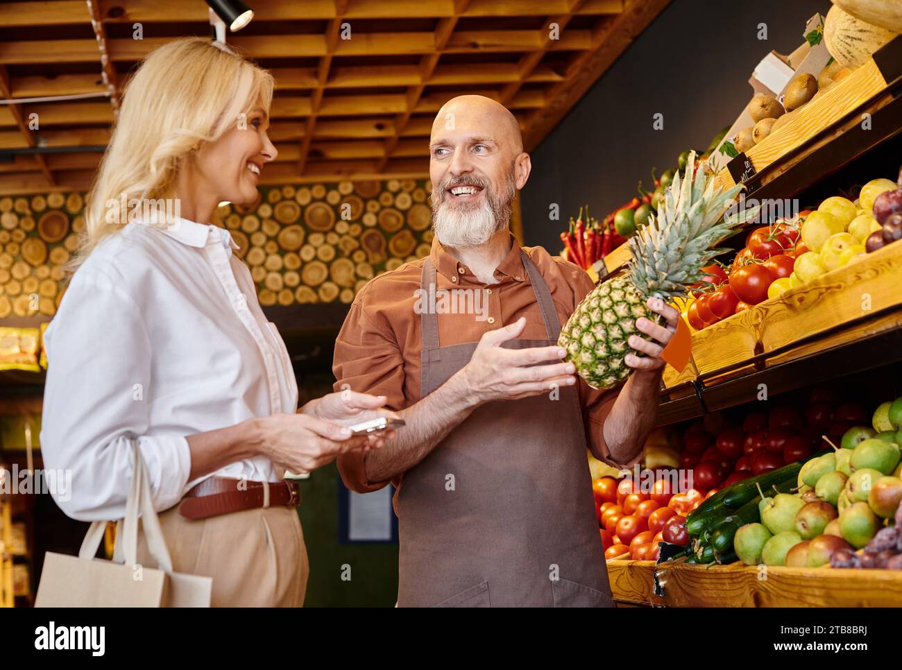 jolly mature salesman with beard showing pineapple to his joyful female ...