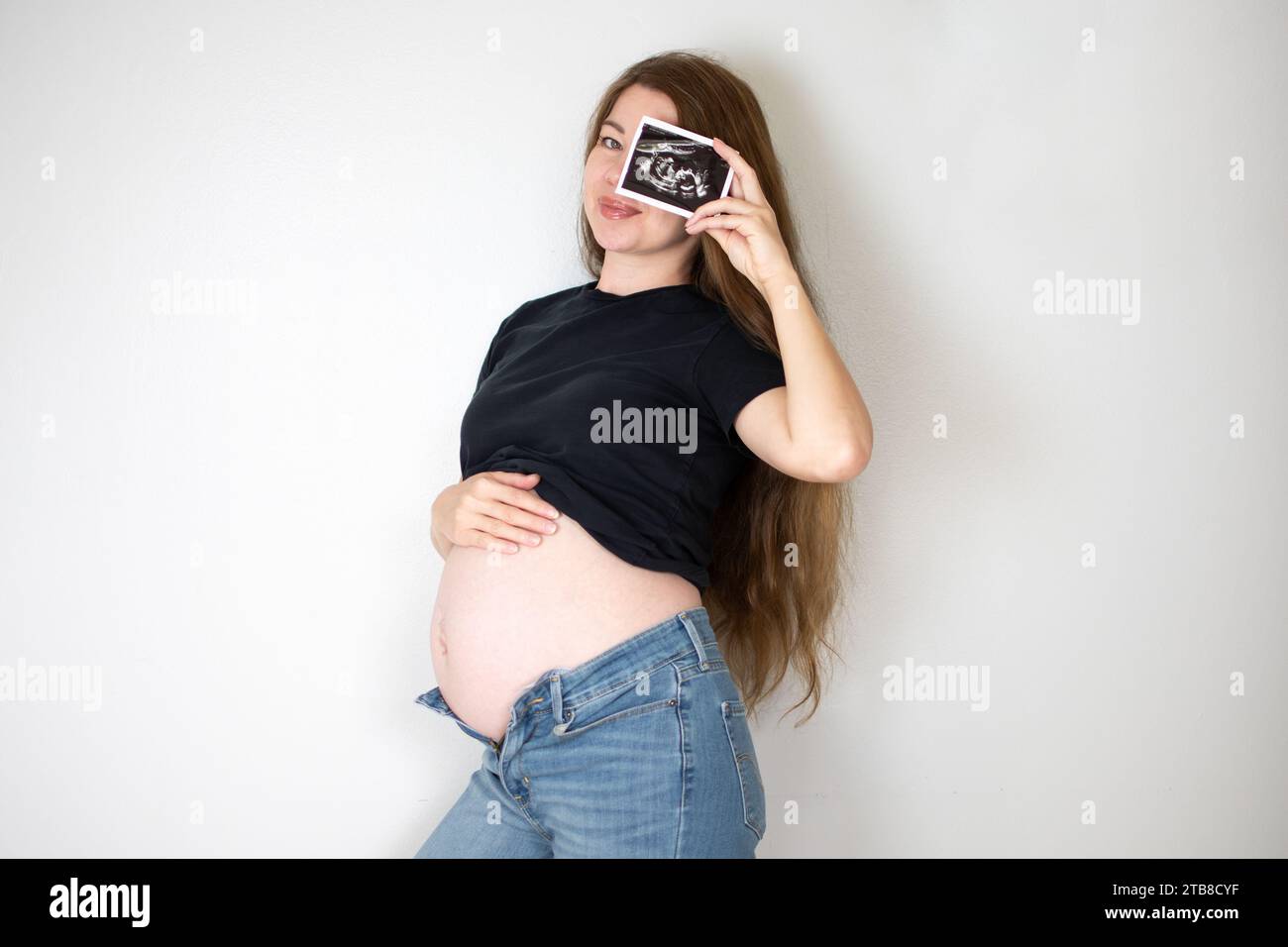 Pregnant Caucasian woman with long hair holding a sonogram picture ...