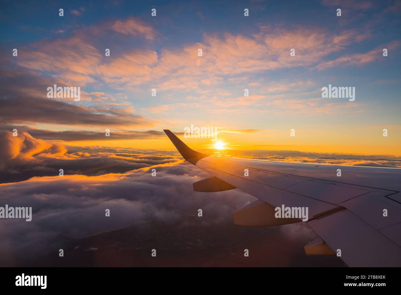 Airplane flight in sunset sky over ocean water and wing of plane. View ...