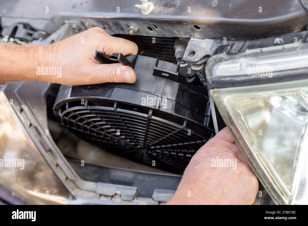 A car mechanic installs a car engine cooling fan under the radiator ...