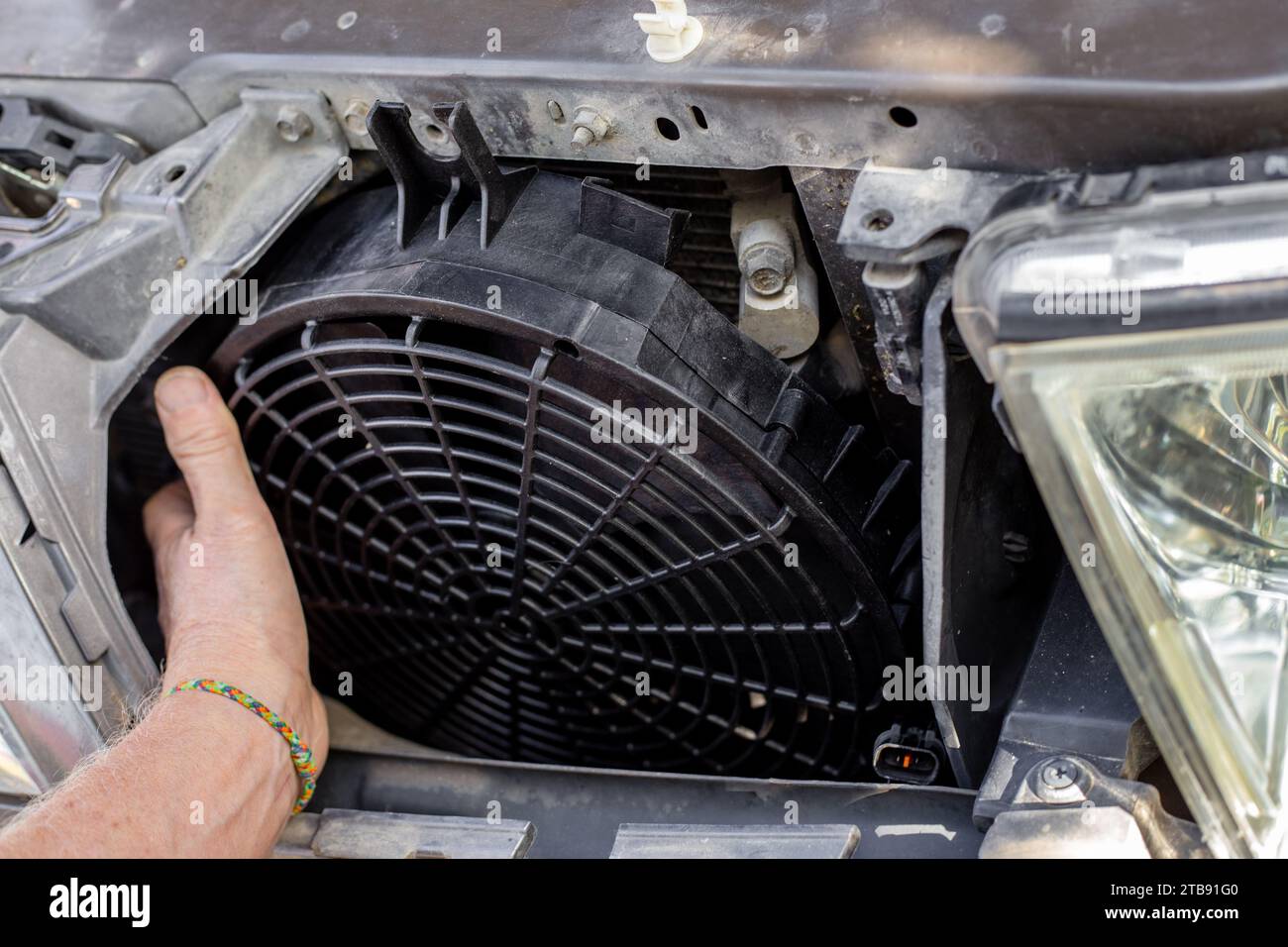 A man fixes an engine cooling fan under the radiator grill of a car ...