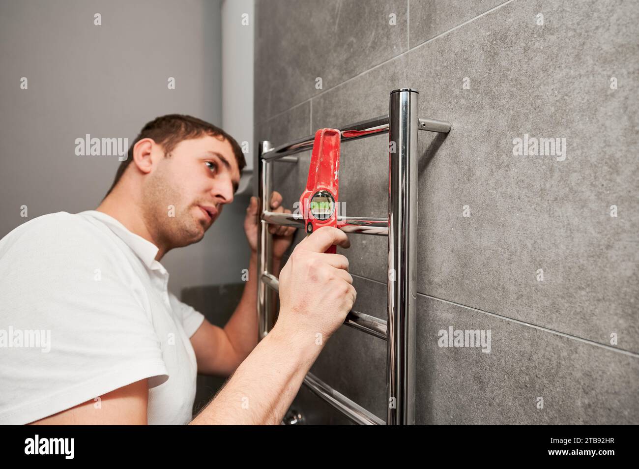 Male plumber checking electric heated towel rack with spirit level ...
