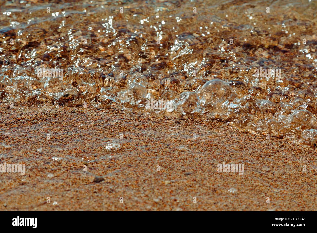 Close up of shallow water on the shore as gentle waves break over warm ...