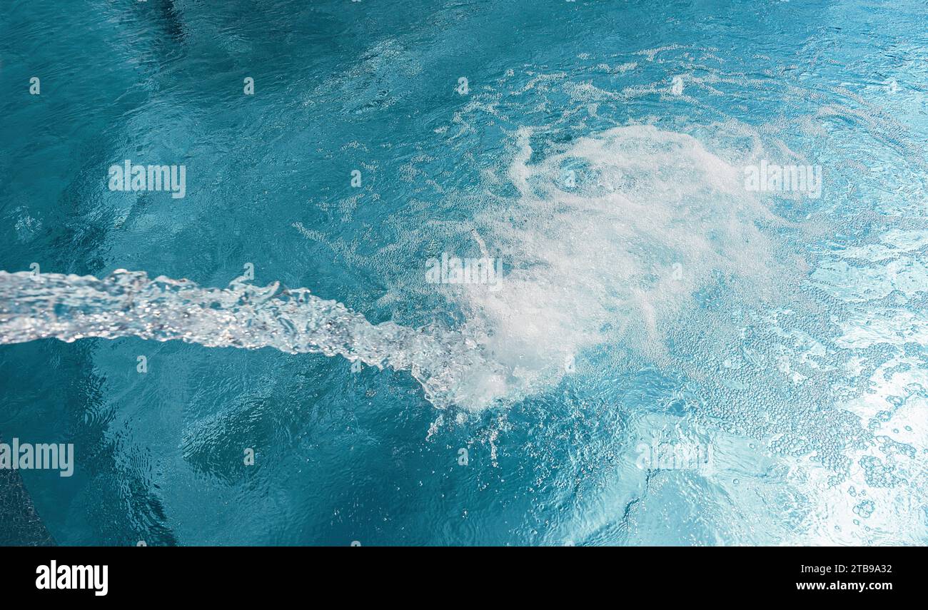 Stream of water hitting the surface of a swimming pool creating bubbles ...