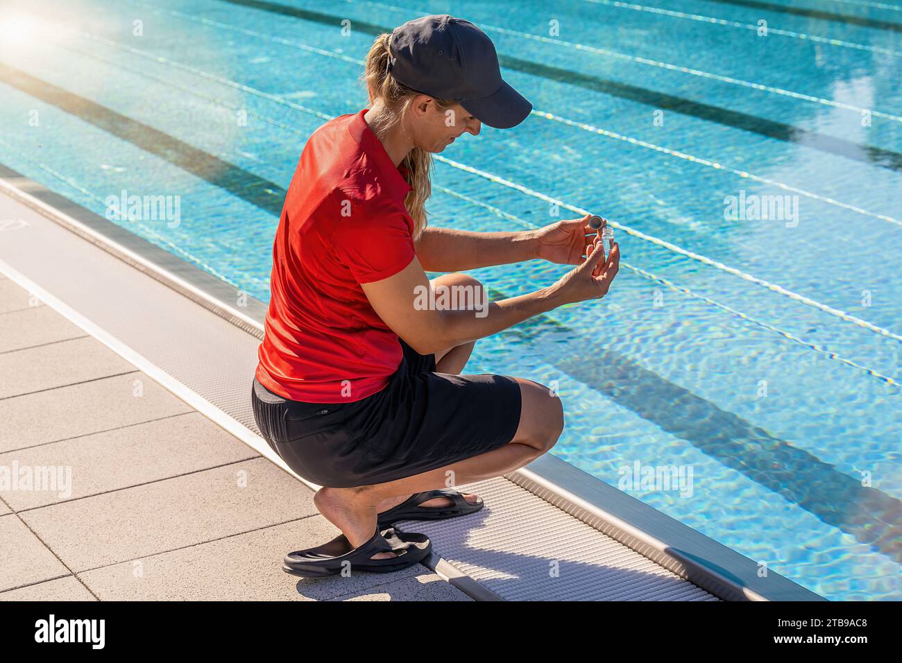 Technician squatting by a pool while examining a water sample in a ...