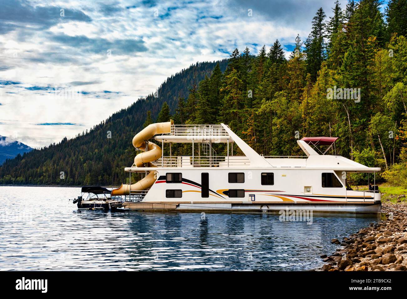 A vacation houseboat parked at a dock on the shoreline of Shuswap Lake ...