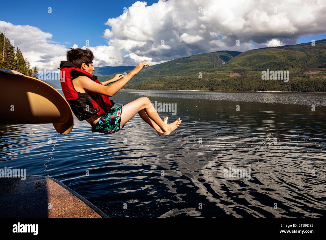 Boy sliding out of the end of a waterslide on a houseboat on a fall day ...