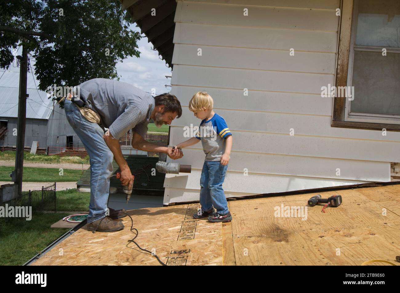 Young boy helping his father replace the roof of an old farmhouse ...
