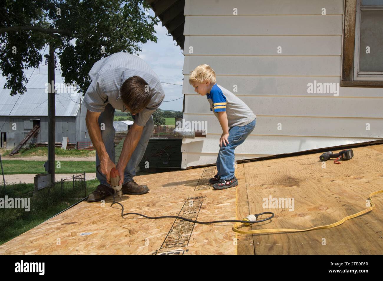Young boy watches his father replace the roof of an old farmhouse ...