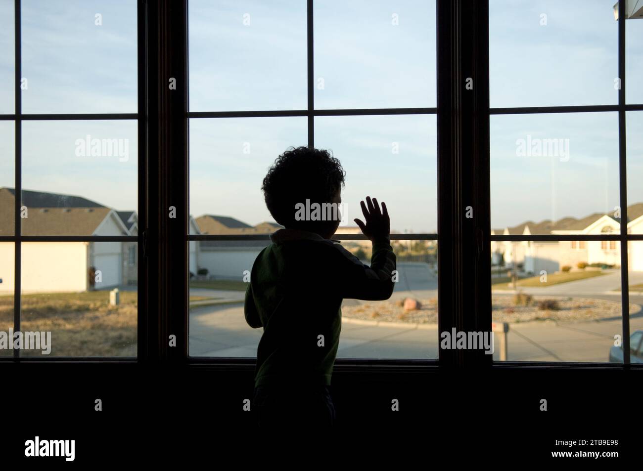 Toddler boy looks out the window of his home to the neighbourhood ...