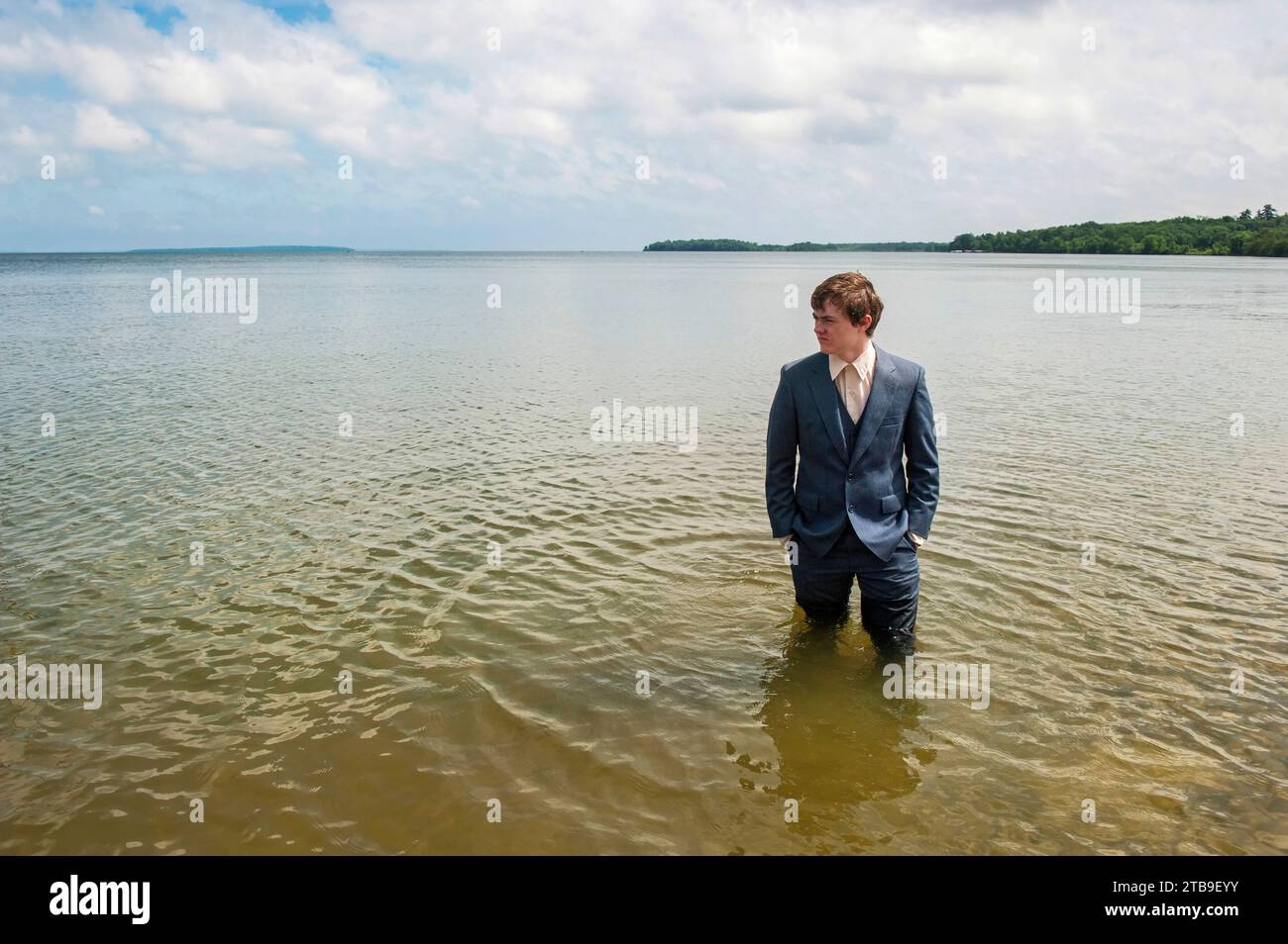Young man wears a suit and stands in a lake; Minnesota, United States ...