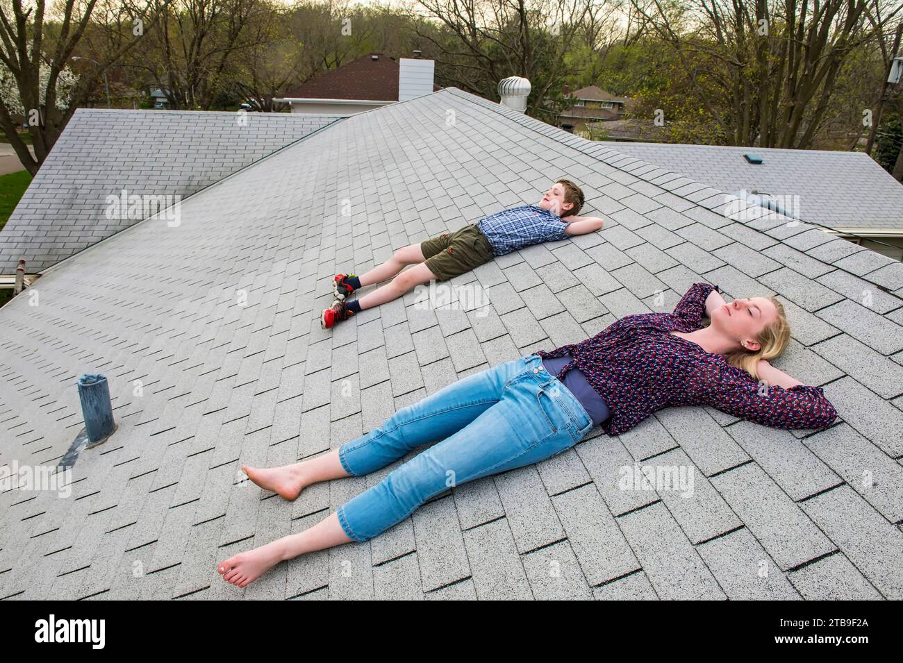 Brother and sister lay on a shingled rooftop; Elkhorn, Nebraska, United ...