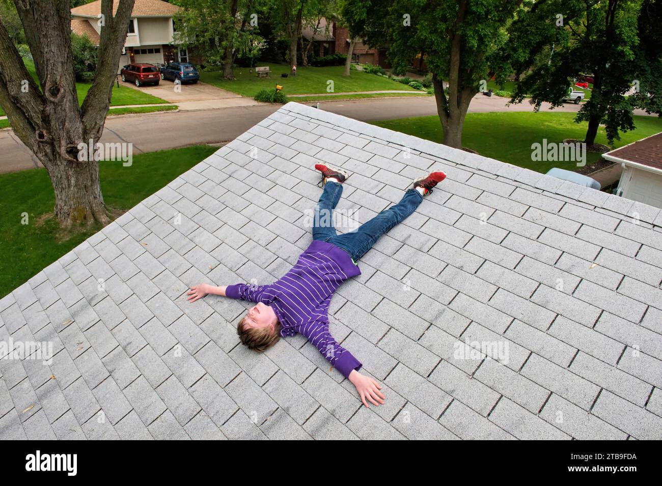 Elementary age boy laying on the shingled roof of a house; Elkhorn ...