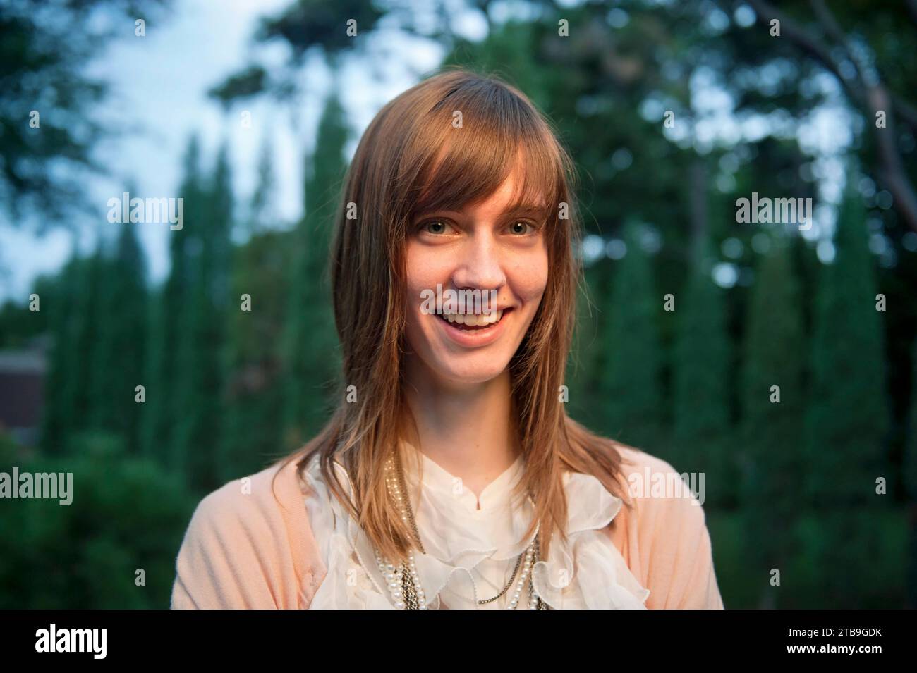 Outdoor portrait of a teenage girl with a big smile, wearing pearls and ...