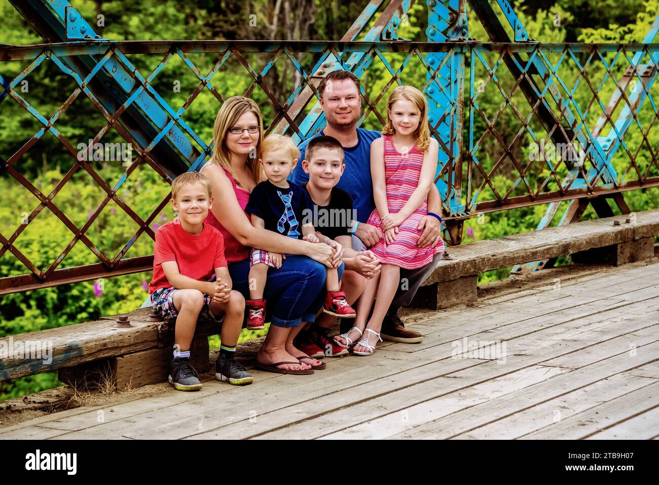 Portrait of a smiling family sitting on a trestle walkway in a park in ...